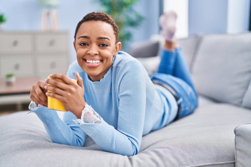 African American Woman Drinking Coffee Lying On Sofa At Home Stock