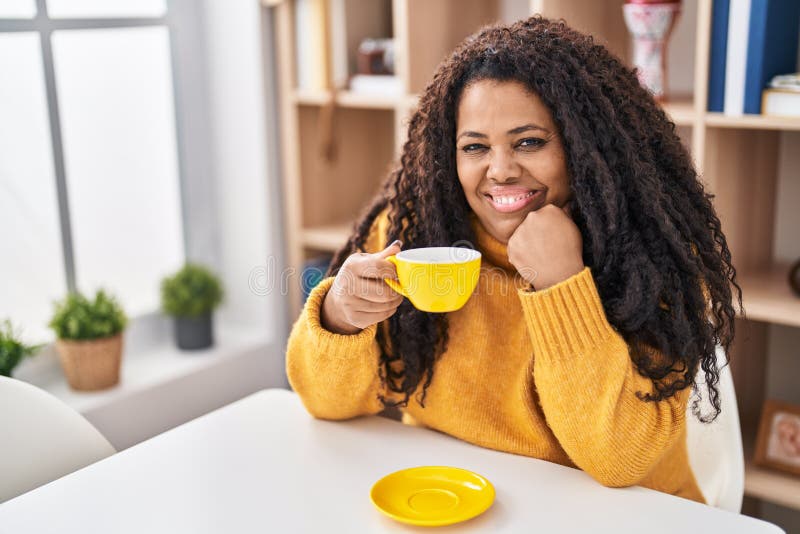 African American Woman Drinking Coffee Sitting On Table At Home Stock
