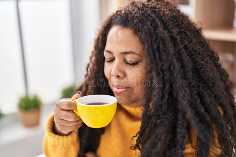 African American Woman Drinking Coffee Sitting On Table At Home Stock