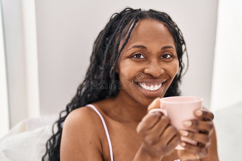 African American Woman Drinking Cup Of Coffee Sitting On Bed At Bedroom