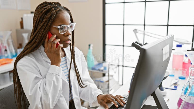 African American Woman in Lab Coat Using Computer and Phone in ...