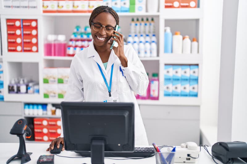 African American Woman Pharmacist Talking on Smartphone Using Computer ...