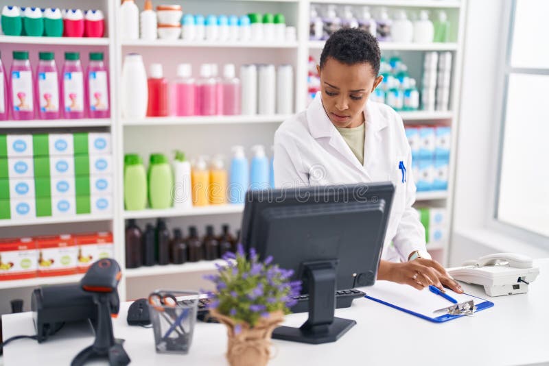 African American Woman Pharmacist Writing on Document Using Computer at ...