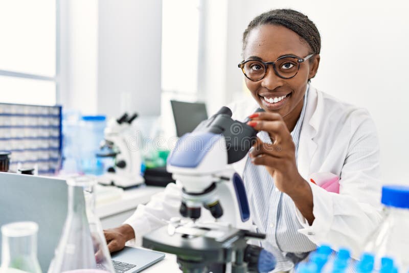 African American Woman Scientist Using Laptop and Microscope at ...