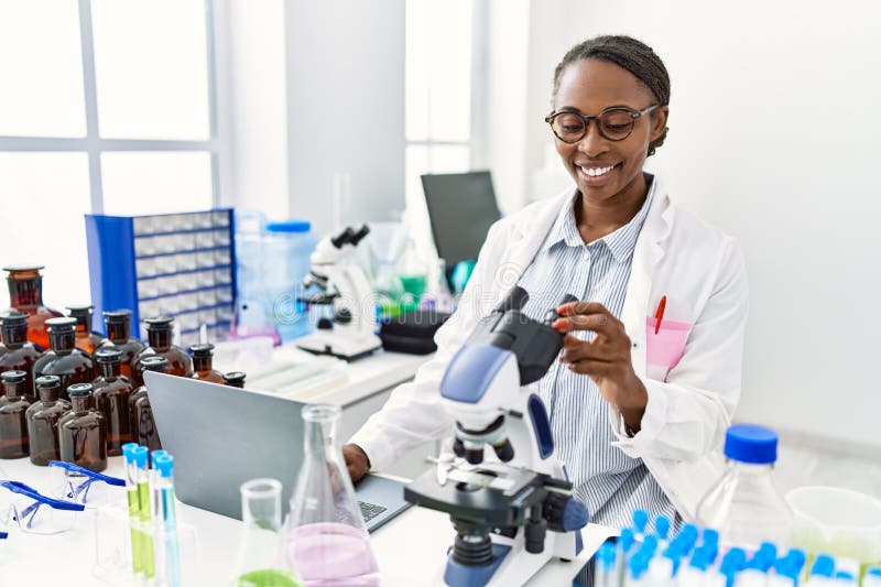 African American Woman Scientist Using Laptop and Microscope at ...