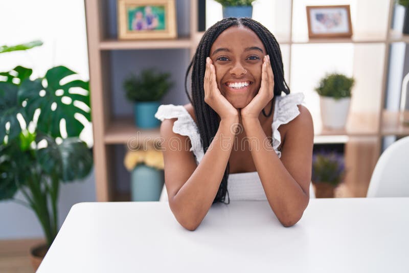 African American Woman Smiling Confident Sitting On Table At Home Stock