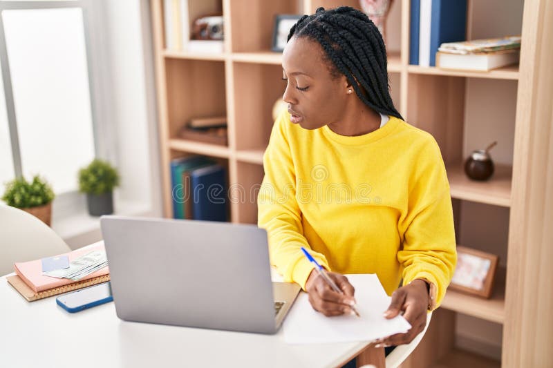 African American Woman Using Laptop Writing on Document at Home Stock ...