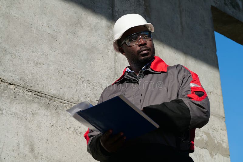 African American Worker Stands at Construction Site with Work Papers ...