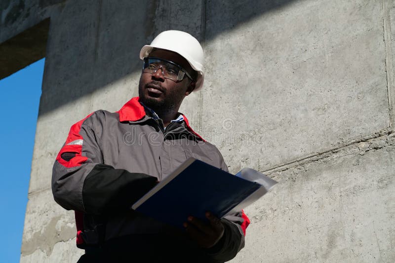 African American Workman Stands at Construction Site with Work Papers ...