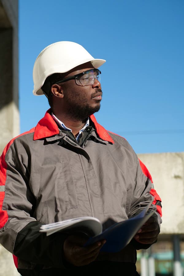 African American Worker Stands at Construction Site with Work Papers ...