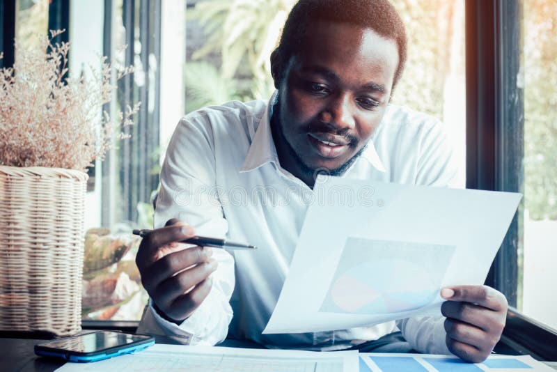 African Business Man Holding Pen and Paperwork and Thinking in Cafe ...