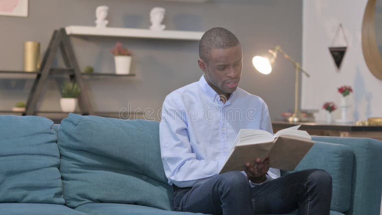 African Man Reading Book while Sitting on Sofa Stock Photo - Image of ...