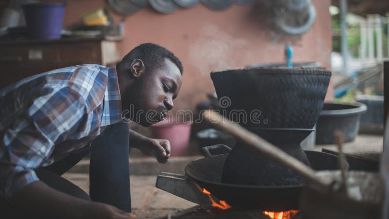 African Man Sitting To Blow Fire To Cook Rice.16:9 Style Stock Photo ...