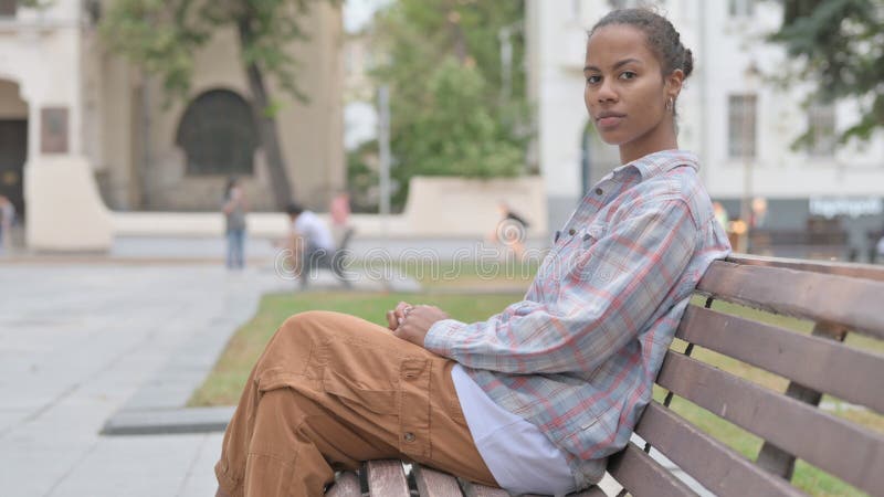 African Woman Looking at Camera while Sitting on Bench Stock Photo ...