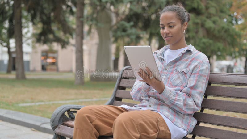 African Woman Using Tablet while Sitting Outdoor on Bench Stock Photo ...