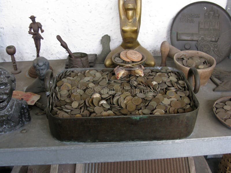 Aged Metal Tray Overflowing with Coins beside Statues on Workshop Shelf ...