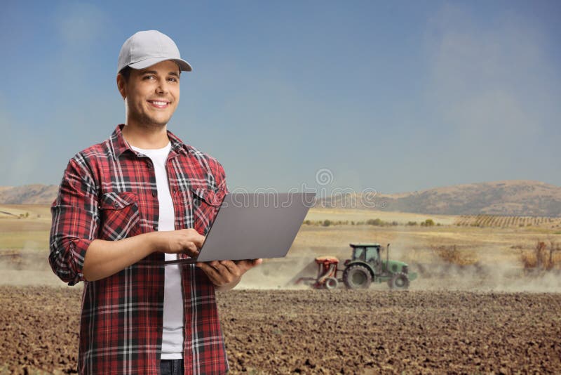 Agricultural Engineer in a Field with a Laptop and a Tractor Plowing ...