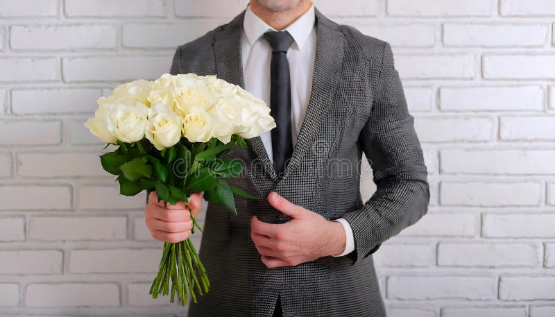 A Man in a Suit and Tie Stands Holding a Bouquet of White Roses. Stock ...