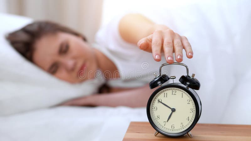 Alarm Clock Opposite Of Sleepy Young Woman Stretching Hand To Ringing