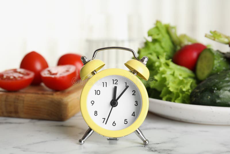Alarm Clock and Vegetables on White Marble Table. Meal Timing Concept ...