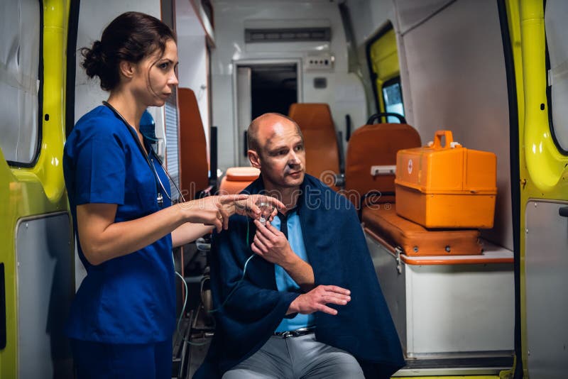 Young Nurse In Uniform Puts Oxygen Mask On Man Sitting In Blanket In