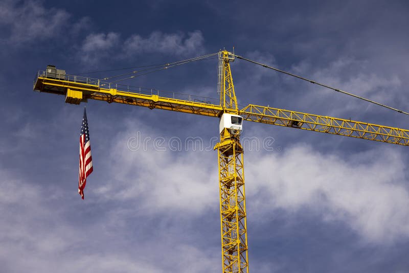An American Flag Hanging Motionless from a Yellow Crane Against a Blue ...