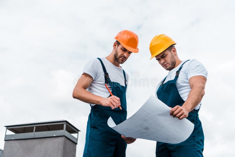 Angle View of Handsome Builders in Uniform and Helmets Looking at Paper ...