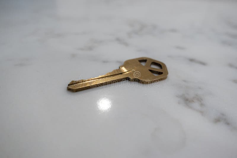 Angled View of a Plain, Bronze Colored Key on Top of a White Marble ...