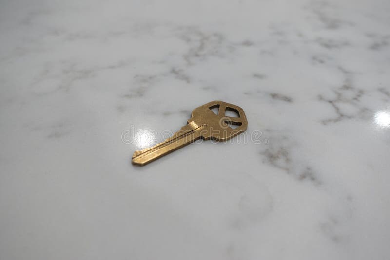 Angled View of a Plain, Bronze Colored Key on Top of a White Marble ...