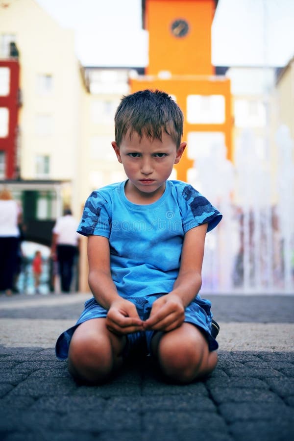 Angry Offended Child Sits on the Ground in the Street and Looks with an ...
