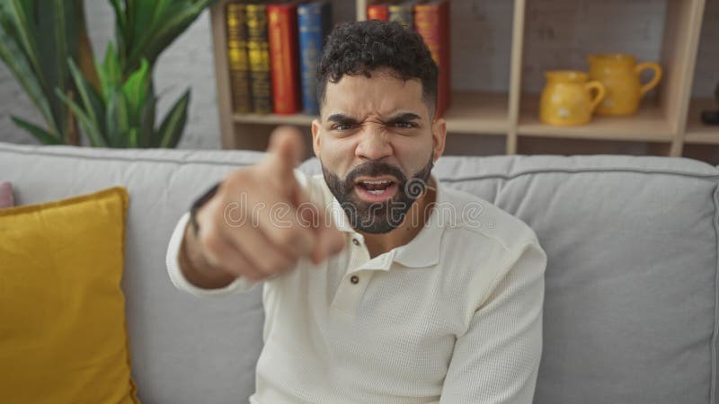 Angry Young Hispanic Man with Beard Pointing at Camera in a Cozy Living ...