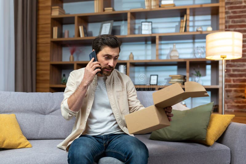 An Angry Young Man is Sitting at Home on the Couch, Holding an Open Box ...