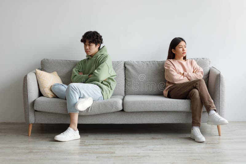 Annoyed Young Asian Couple Sitting On Couch In Silence After Fight