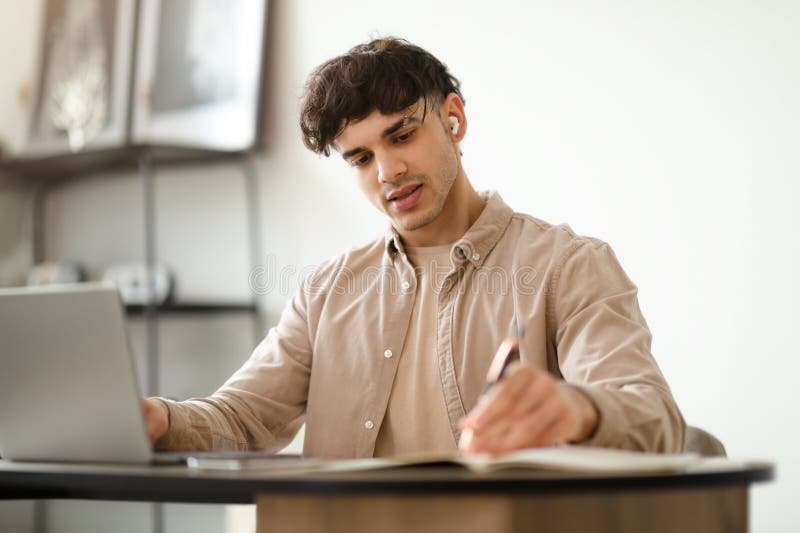 Arab Guy Writing Notes Learning at Laptop Wearing Earphones Indoor ...