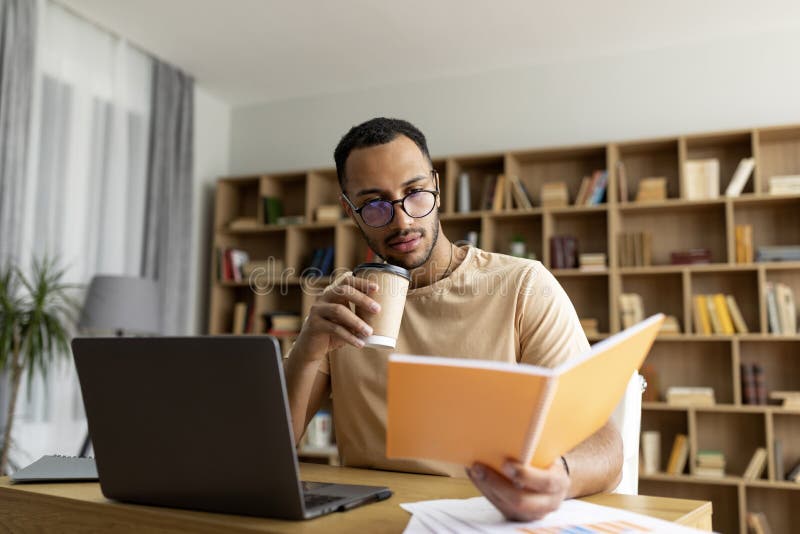Arab Man Studying Online from Home, Reading Notebook and Drinking ...