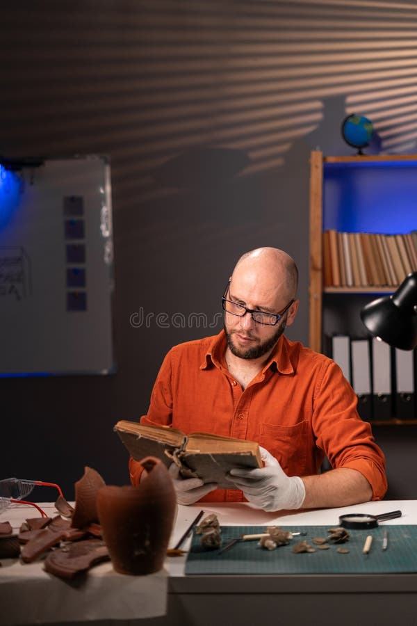 Archaeologist Working Late at Night in the Office Reading an Old Book ...