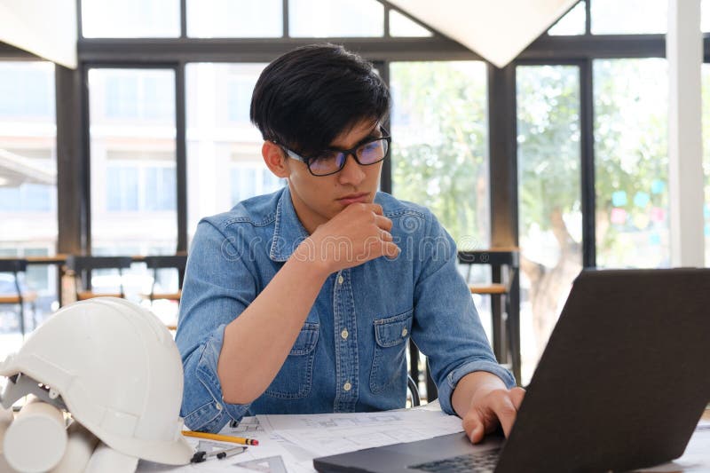 Architect and Engineer Working on a Laptop with Blueprints at a Desk in ...