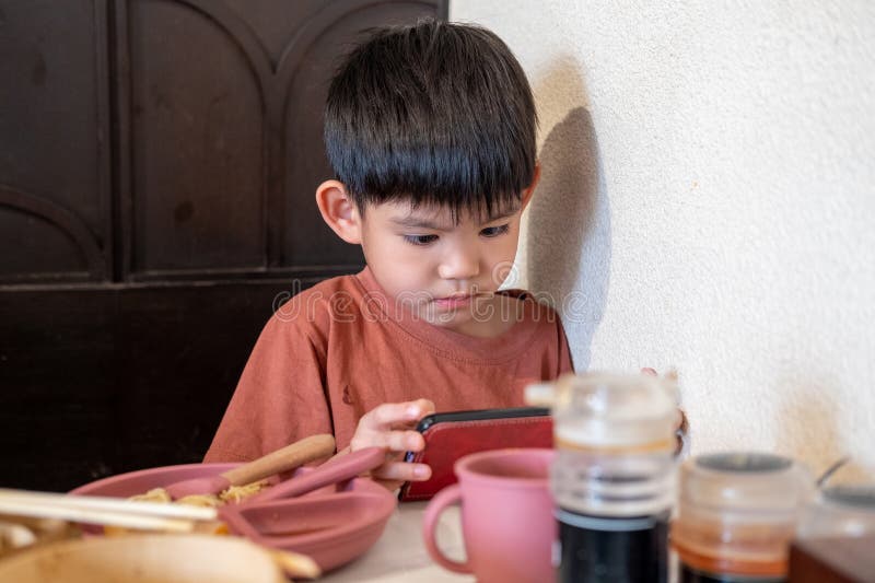 Asian Boy Playing with Mobile Phone while Eating Stock Photo - Image of ...