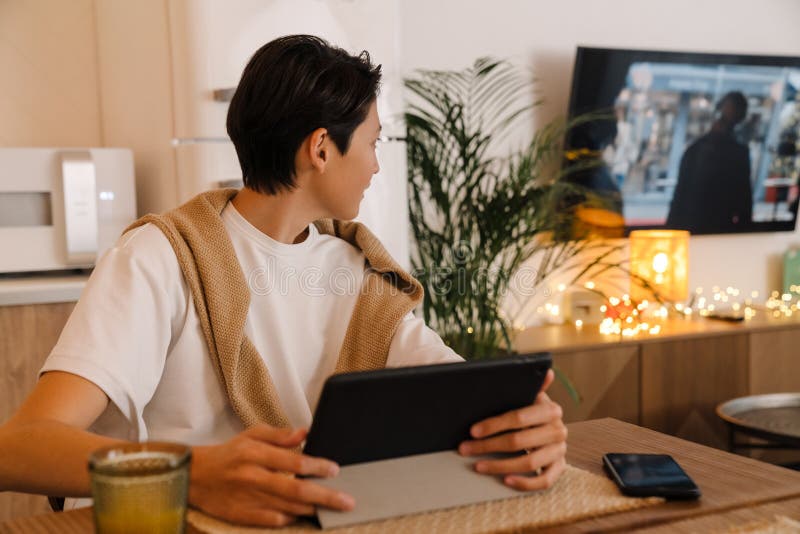 Asian Boy Using Tablet Computer while Watching Tv in Kitchen Stock ...