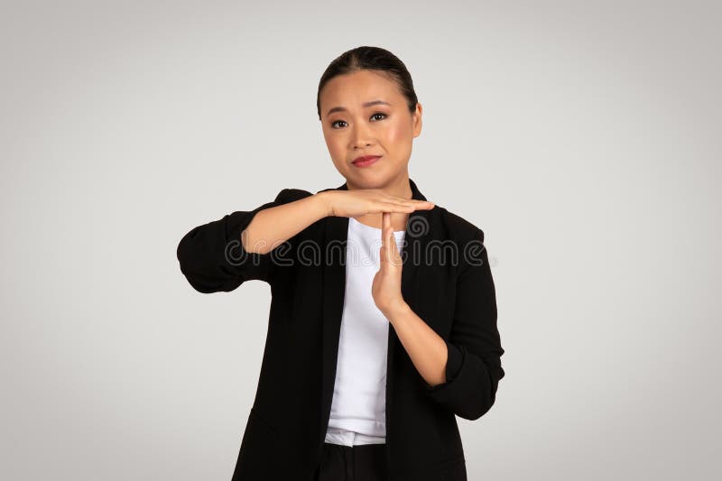 Asian Businesswoman in a Black Suit Making a Timeout Gesture with a Serious Expression Stock ...