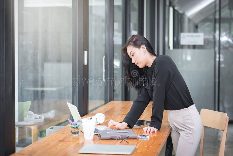 Asian Businesswoman Standing at Table and Using a Laptop in Modern ...
