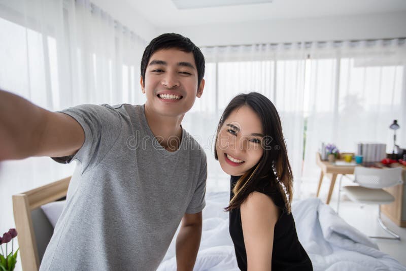 Asian Couple Lovers Lying On Their Play Mobile Phones And Selfie On Bed