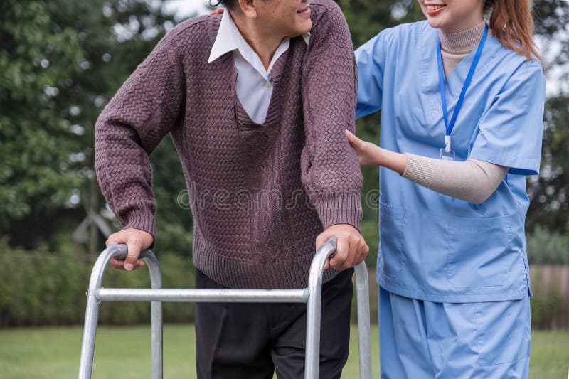 Asian Female Caregiver Helps Senior Man Walk A Senior Using A Walker Is