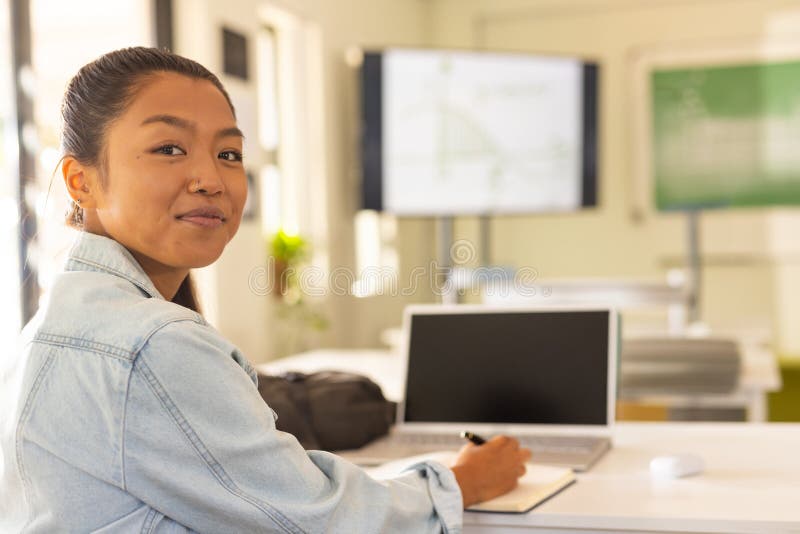 Asian Female Student Writing in Notebook at Desk in Classroom with ...