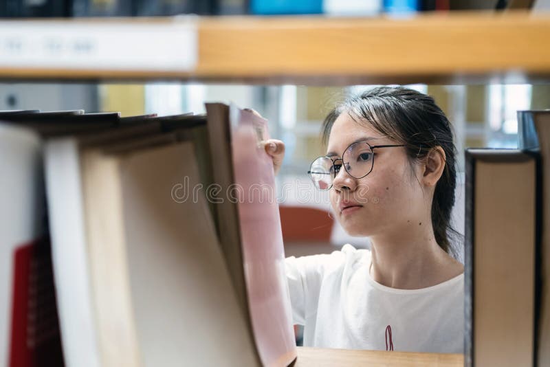 An Asian Girl is Looking at Books on a Shelf in Library Stock Photo ...