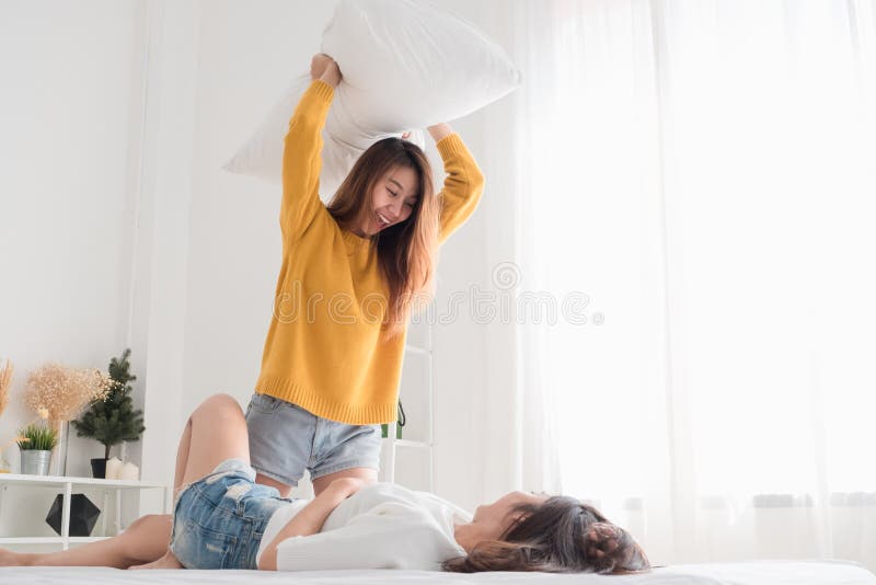 Asian Lesbain Woman Playing Pillow Flight Together On Bed In White