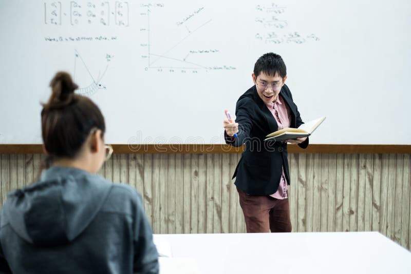 An Asian Male Teacher in a Classroom Near the Whiteboard is Writing and ...