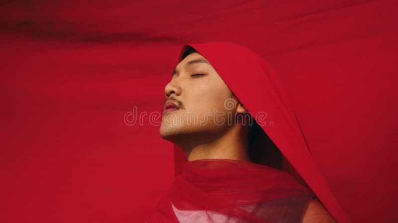 An Asian Man Bound and Strangled by a Red Cloth with a Resigned Face in Front of a Red ...