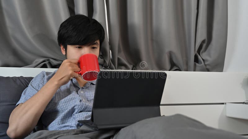 Man Drinking Coffee while Using Computer Tablet on Bed in the Morning ...