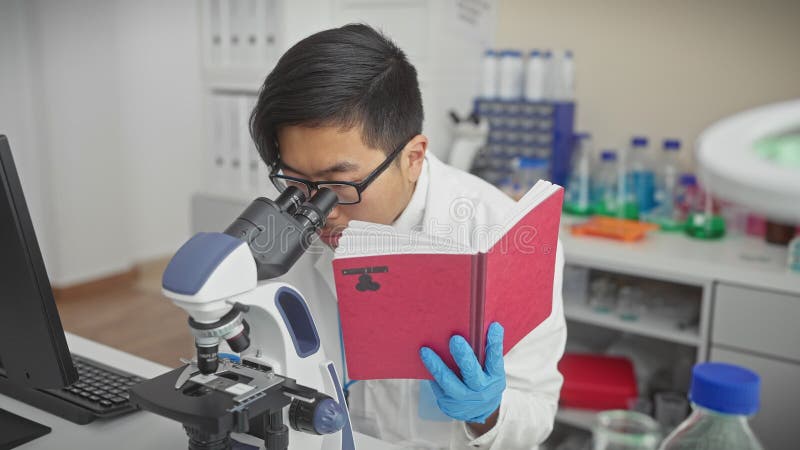 Asian Man Reading a Book while Analyzing Samples Using a Microscope in ...